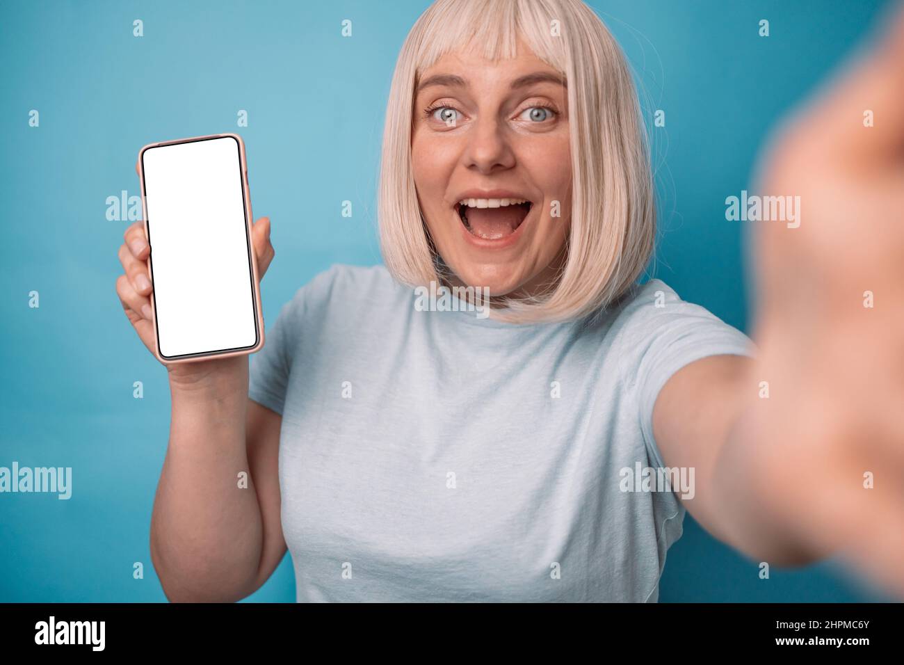 Crazy smiling 20s girl showing empty smart phone screen on blue studio ...