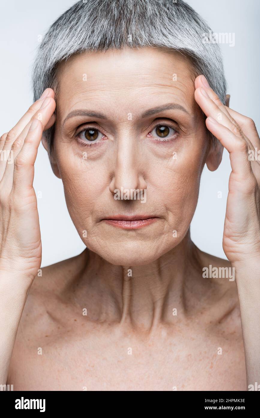 middle aged woman with wrinkles touching temples isolated on grey Stock ...