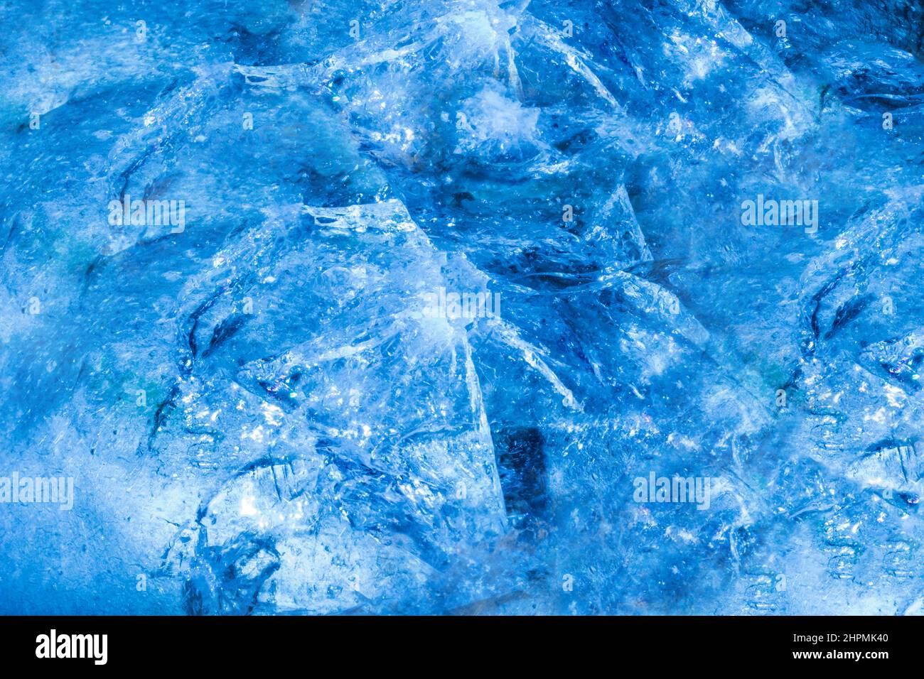 Close up photo of blue toned frozen cracked and damaged ice surface ...