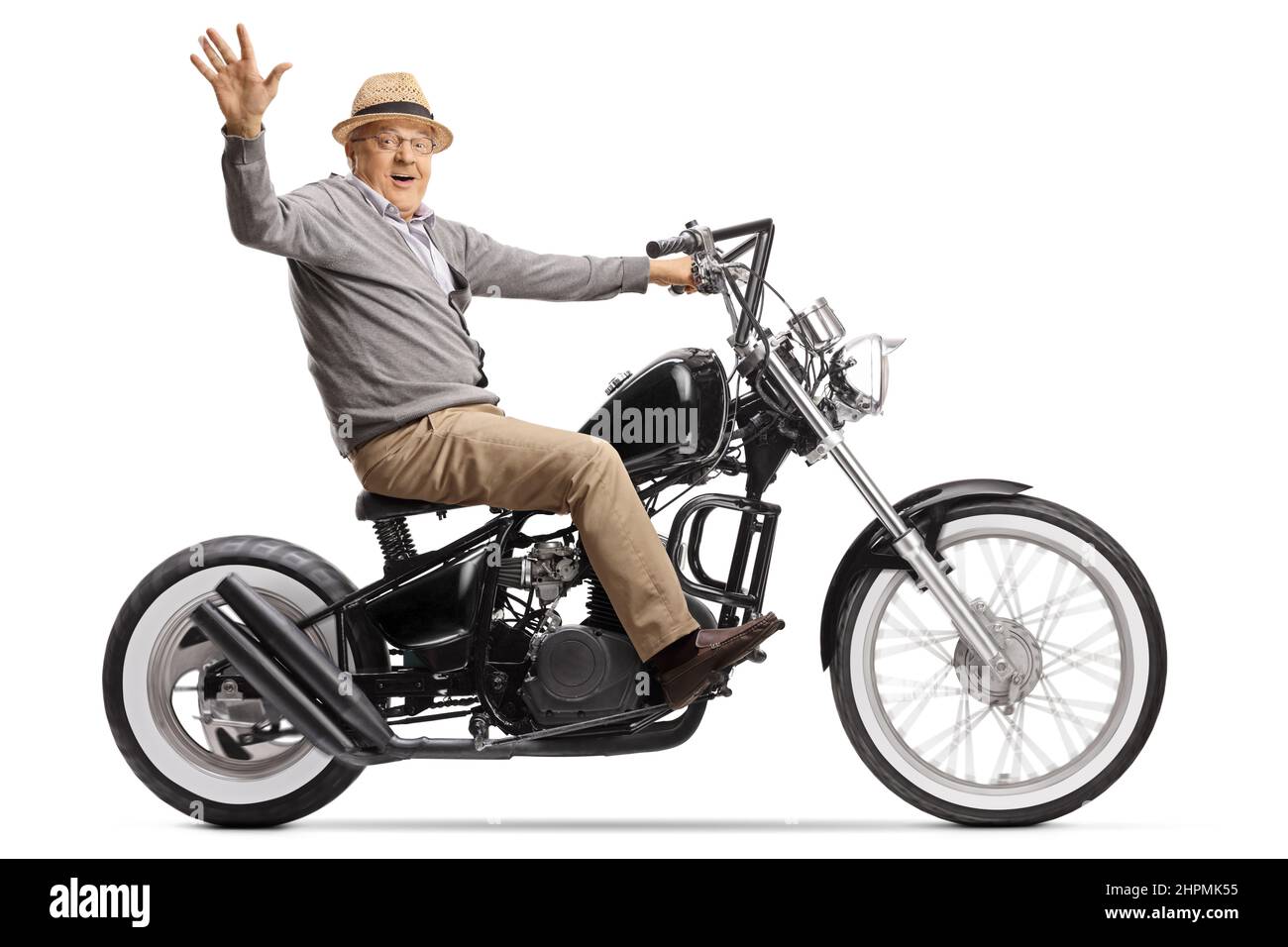 Senior man riding a custom chopper motorbike and waving at the camera ...