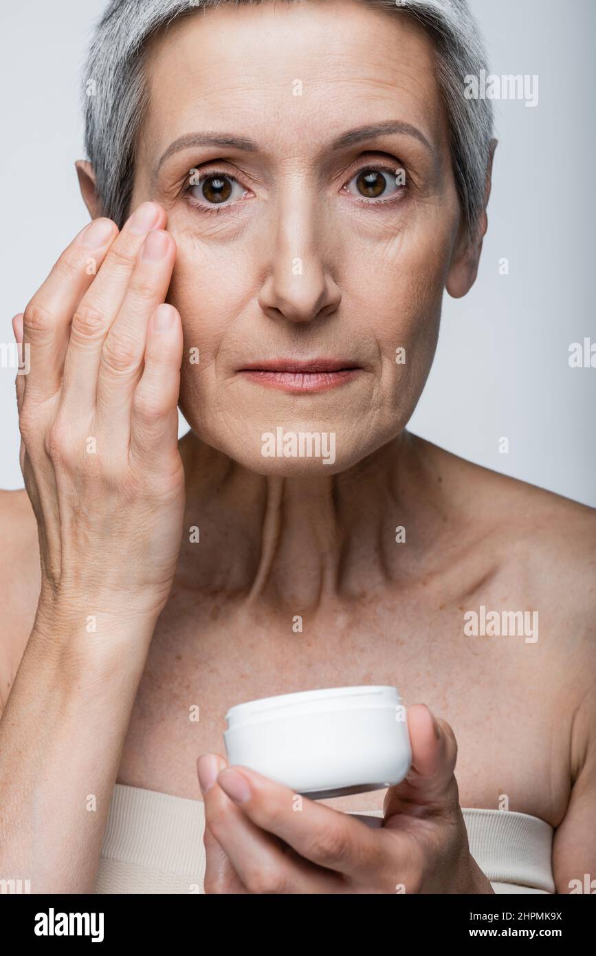 mature woman with grey hair applying anti-wrinkle cream isolated on ...
