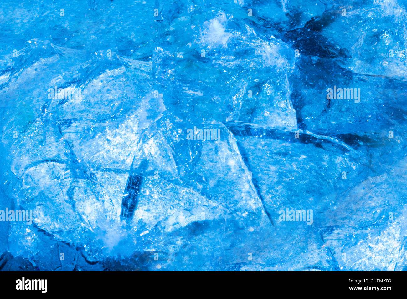 Close up photo of blue toned frozen cracked and damaged ice surface ...