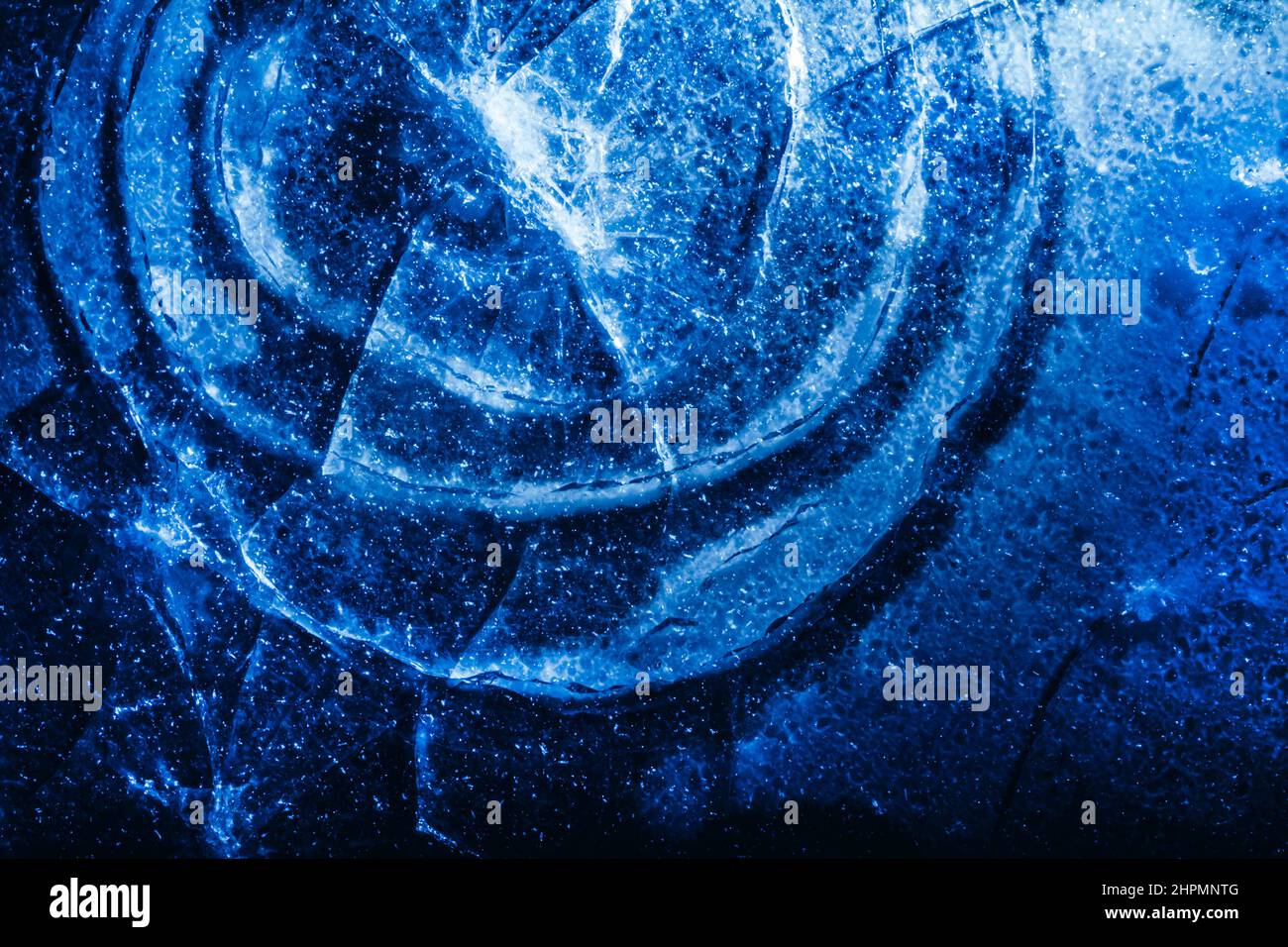 Close up photo of blue toned frozen circle cracked and damaged ice ...
