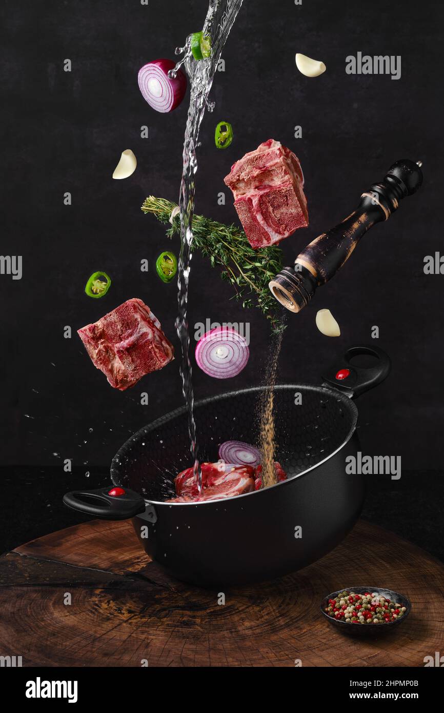 Chopped beef bones falling into saucepan with ingredients for bouillon ...