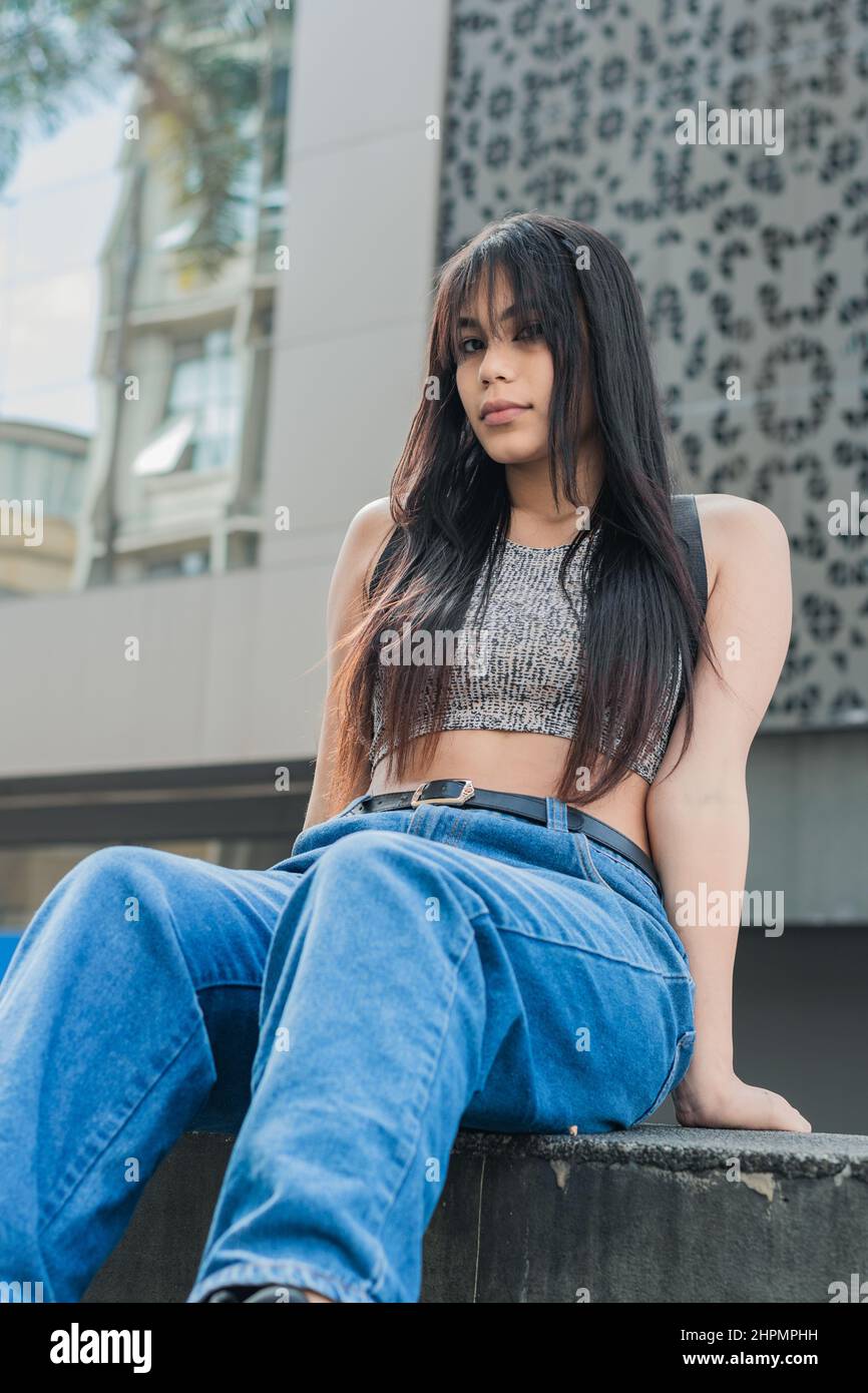 beautiful latina woman with brown skin, sitting on the sidewalk in the ...