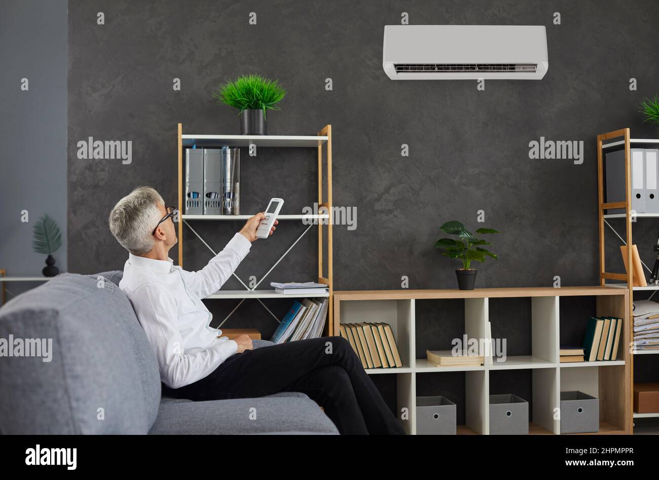 Man sitting on couch in his office switches modern air conditioner with ...