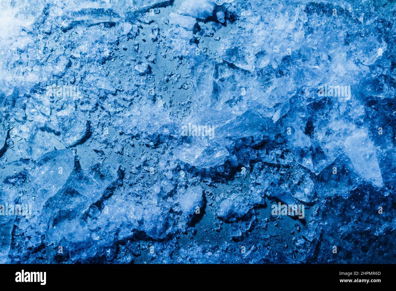 Photo of blue toned frozen cracked ice with snow particles surface ...