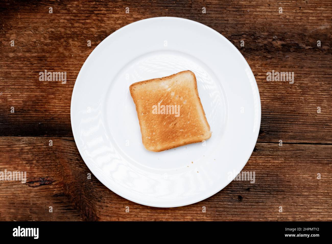 A piece of toasted white toast on a white plate. Dark wooden background ...