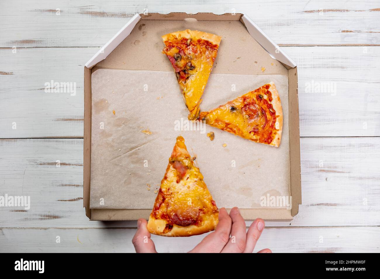 The hand takes a slice of pizza in a cardboard box. white wood ...