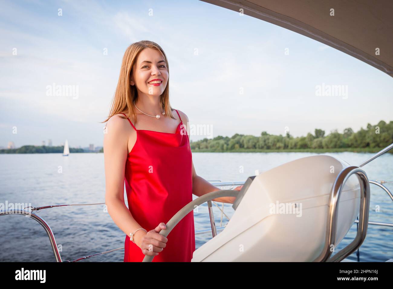 Beautiful lady skipper in a long red dress holding the helm of the ship ...