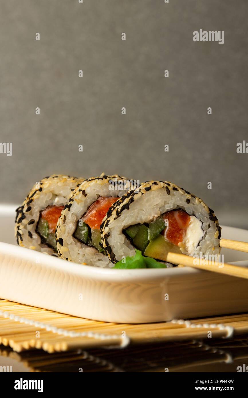 Fresh and tasty sushi rolls lie on a white dish and a bamboo mat on a ...