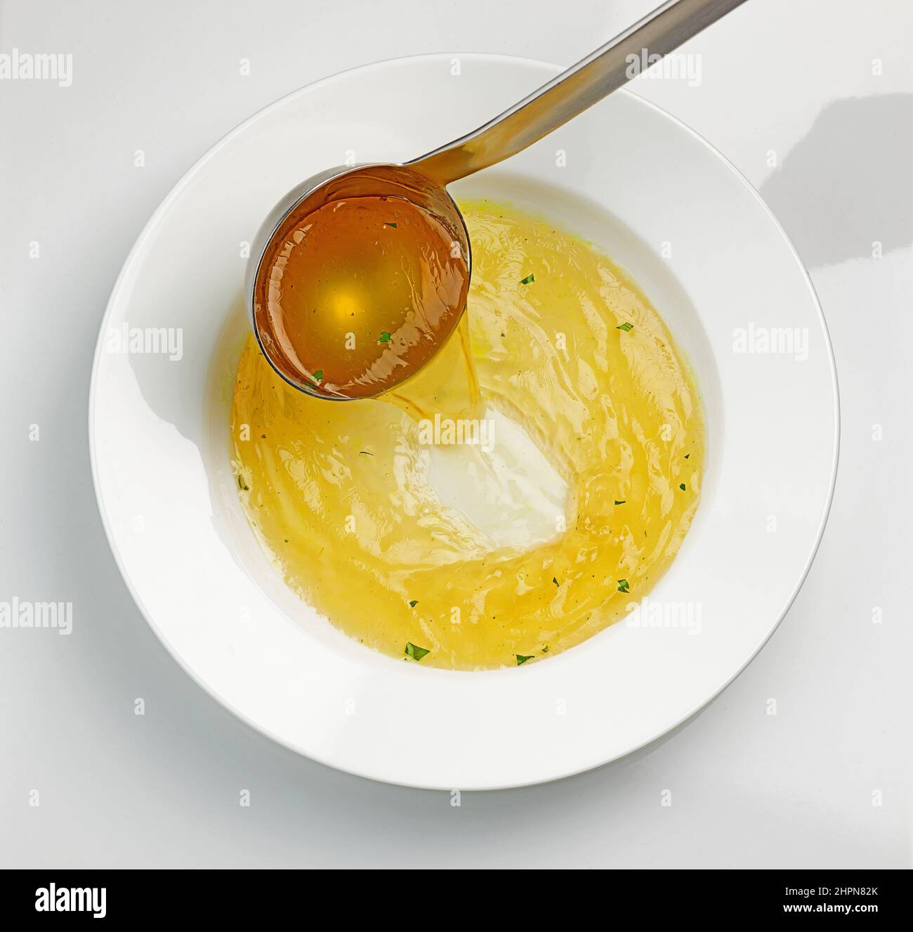 chicken broth pouring into soup plate on white kitchen table, top view ...