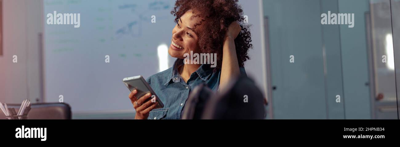 Smiling young lady using mobile phone in the office Stock Photo - Alamy