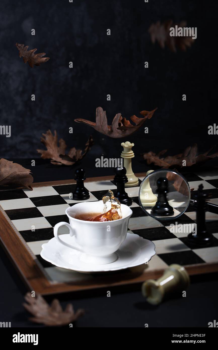 A cup of tea with a splash, falling autumn leaves on a chess table ...