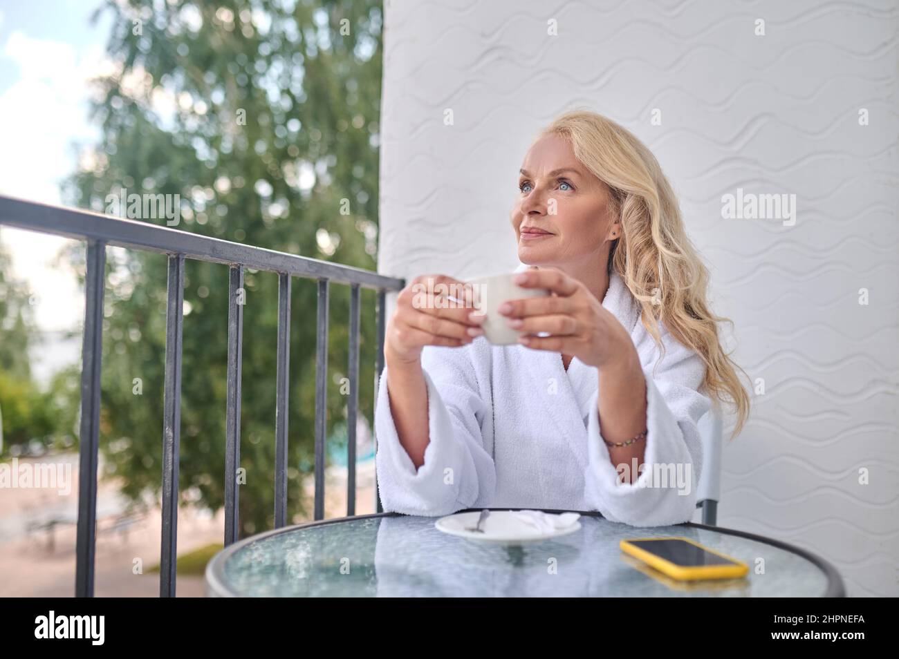 A blonde woman in a white robe sitting and working on a laptop Stock ...