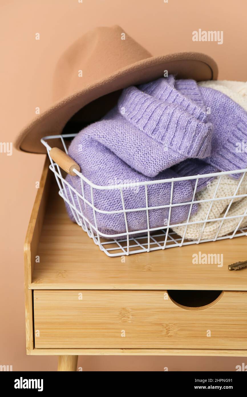 Basket with knitted sweaters and hat on table near beige wall Stock ...