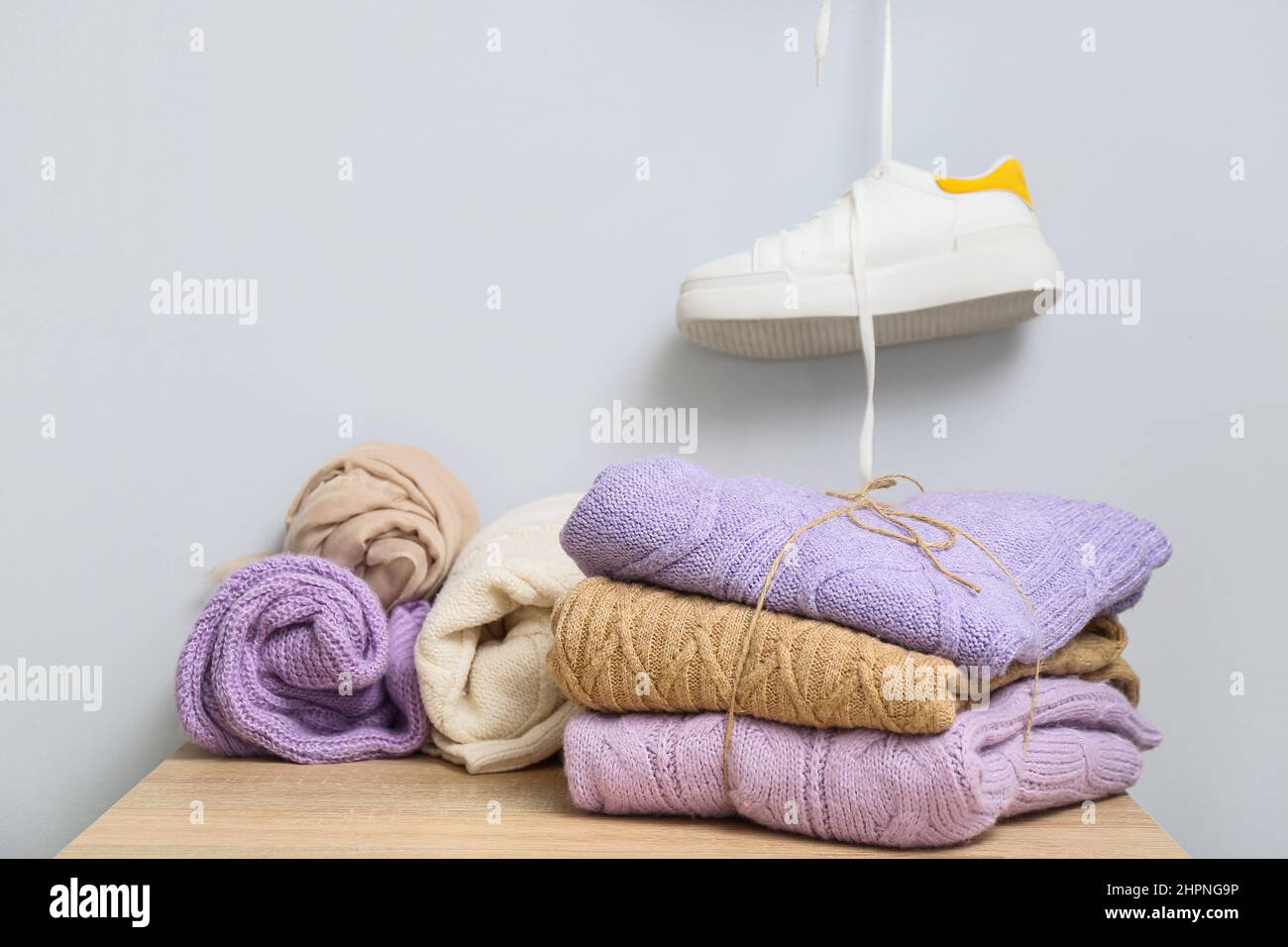 Folded sweaters on table and sneaker hanging on light wall Stock Photo ...