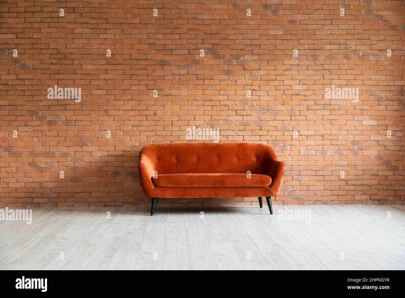 Red sofa near brick wall in empty room Stock Photo - Alamy