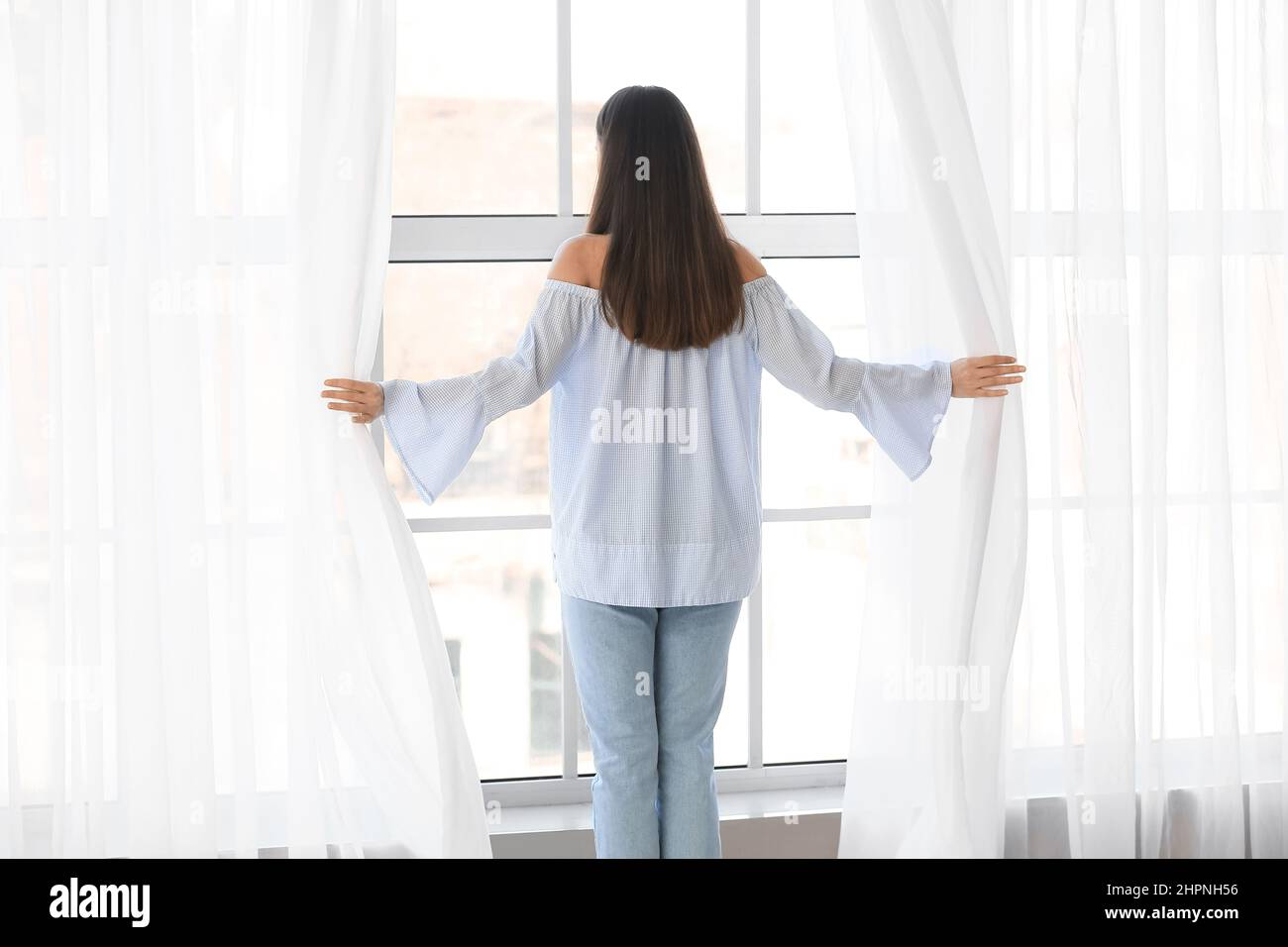 Pretty young woman opening curtains in room Stock Photo - Alamy
