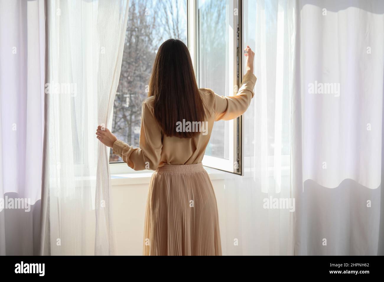 Pretty young woman opening window in room Stock Photo - Alamy