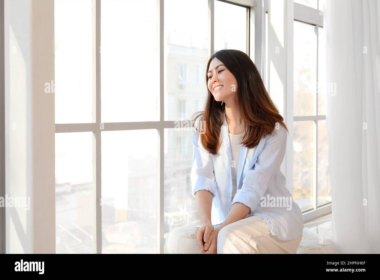 Pretty young Asian woman sitting on window sill Stock Photo - Alamy