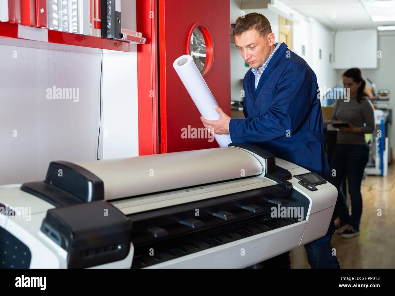 Worker loads new roll of paper into the plotter Stock Photo - Alamy