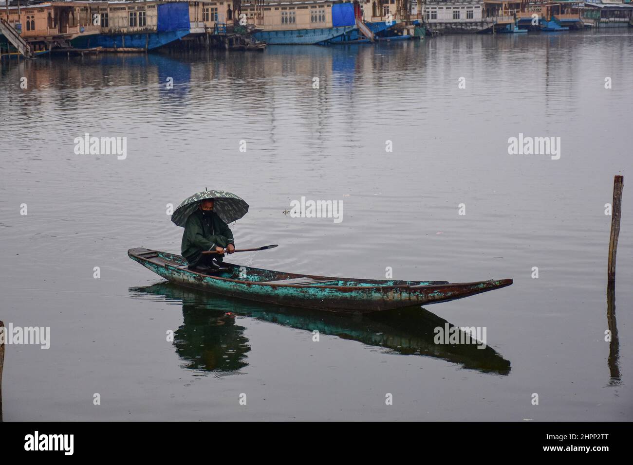 A boatman holds an umbrella as he rows his boat across the Dal lake ...