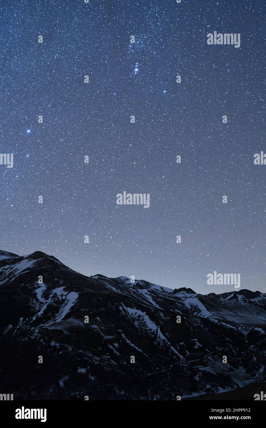 Vertical shot of a slope of a snowy mountain under the starry night sky ...