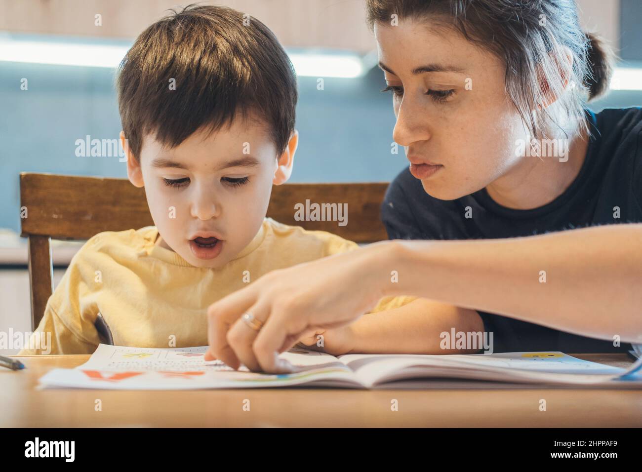 Mother helping with homework her son pointing to something written in his notebook. Mom help boy ...
