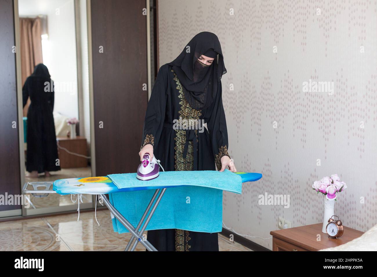 A Muslim woman in national clothes is doing household chores ironing a ...