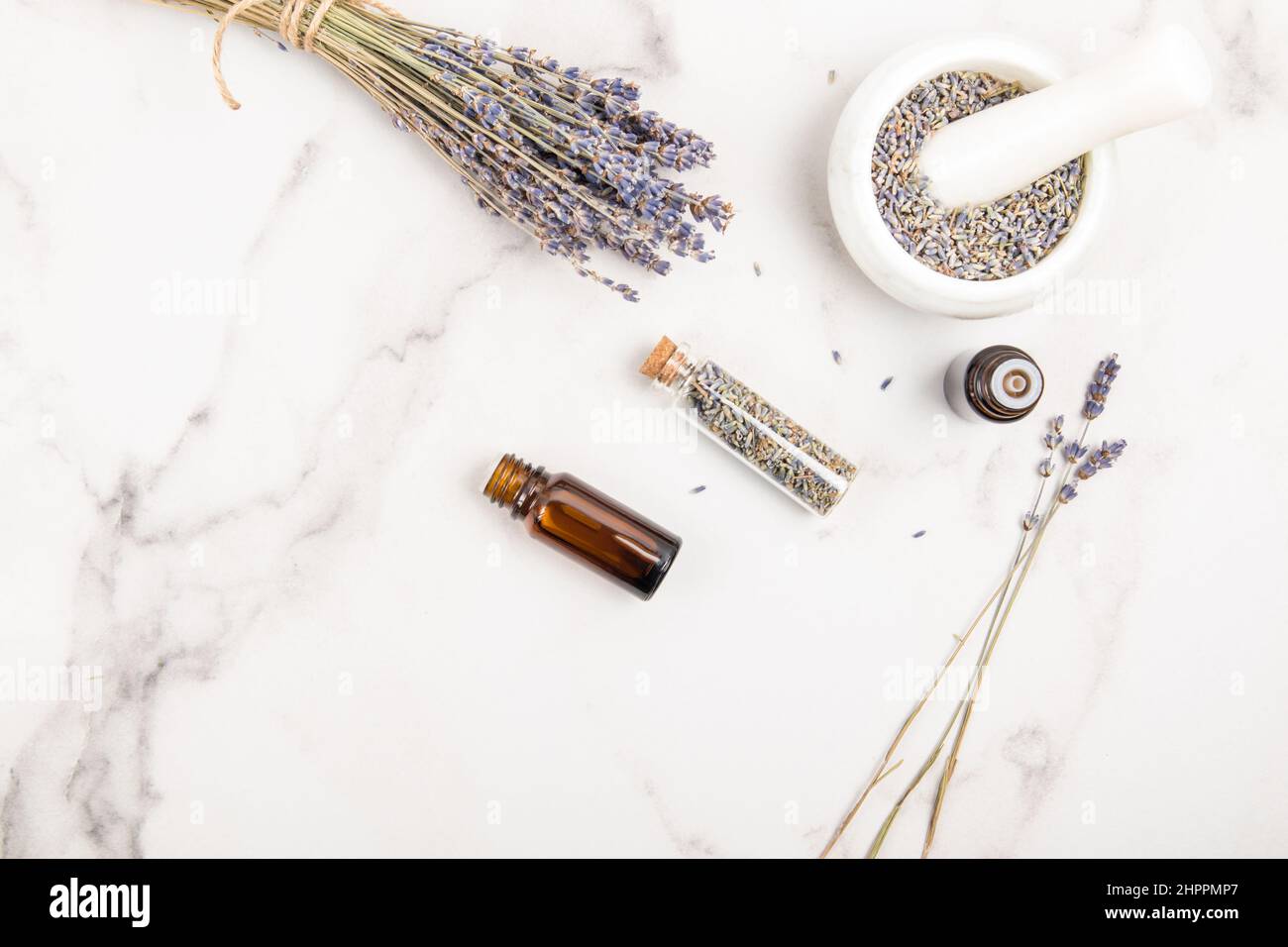 lavender essential oil, plant flowers and seeds in a mortar with a pestle on a marble table ...