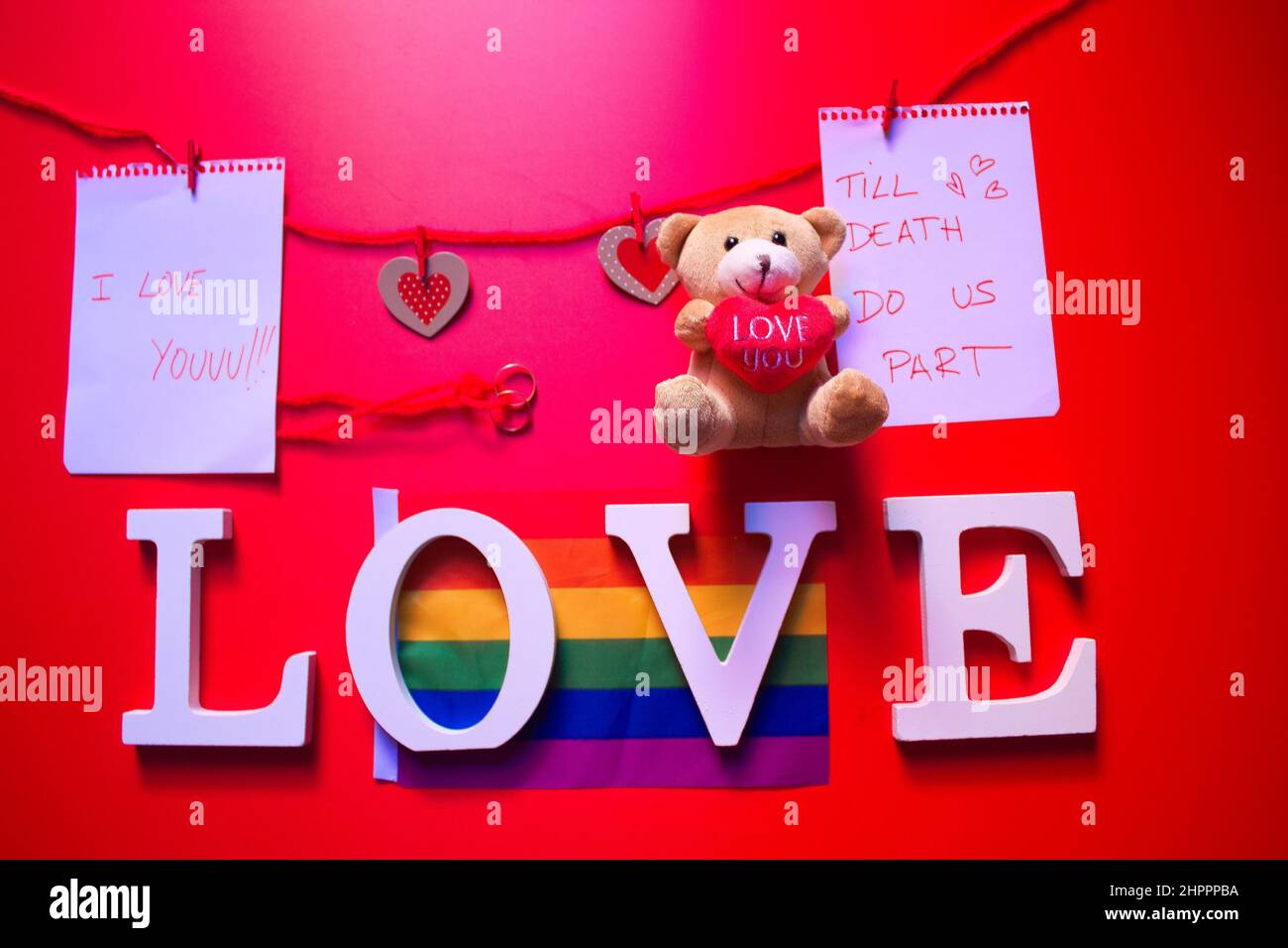 Closeup of love notes with gifts and a pride flag on a red surface ...