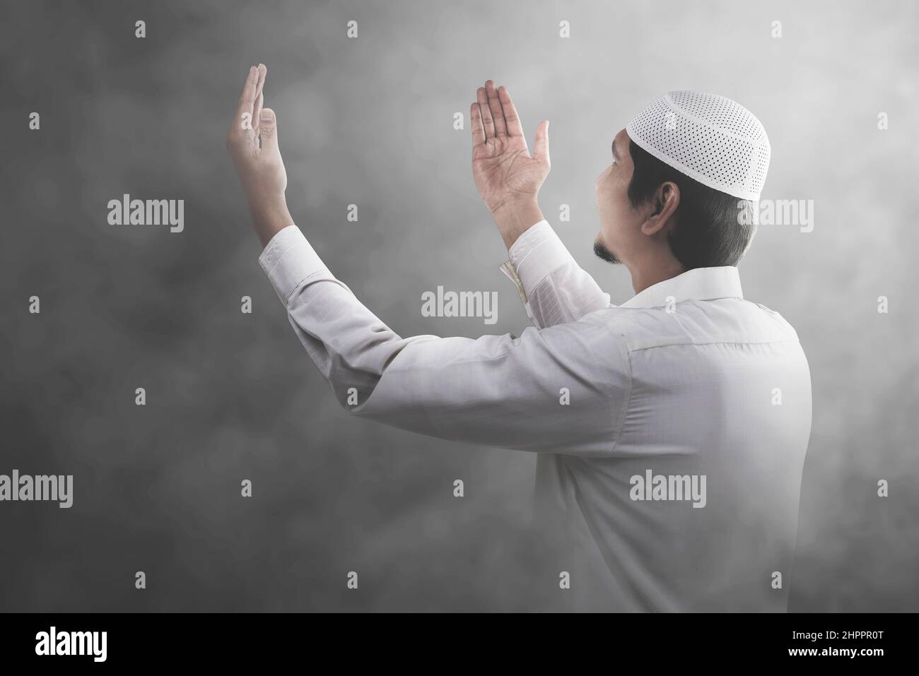 Asian Muslim man standing while raised hands and praying with bright ...