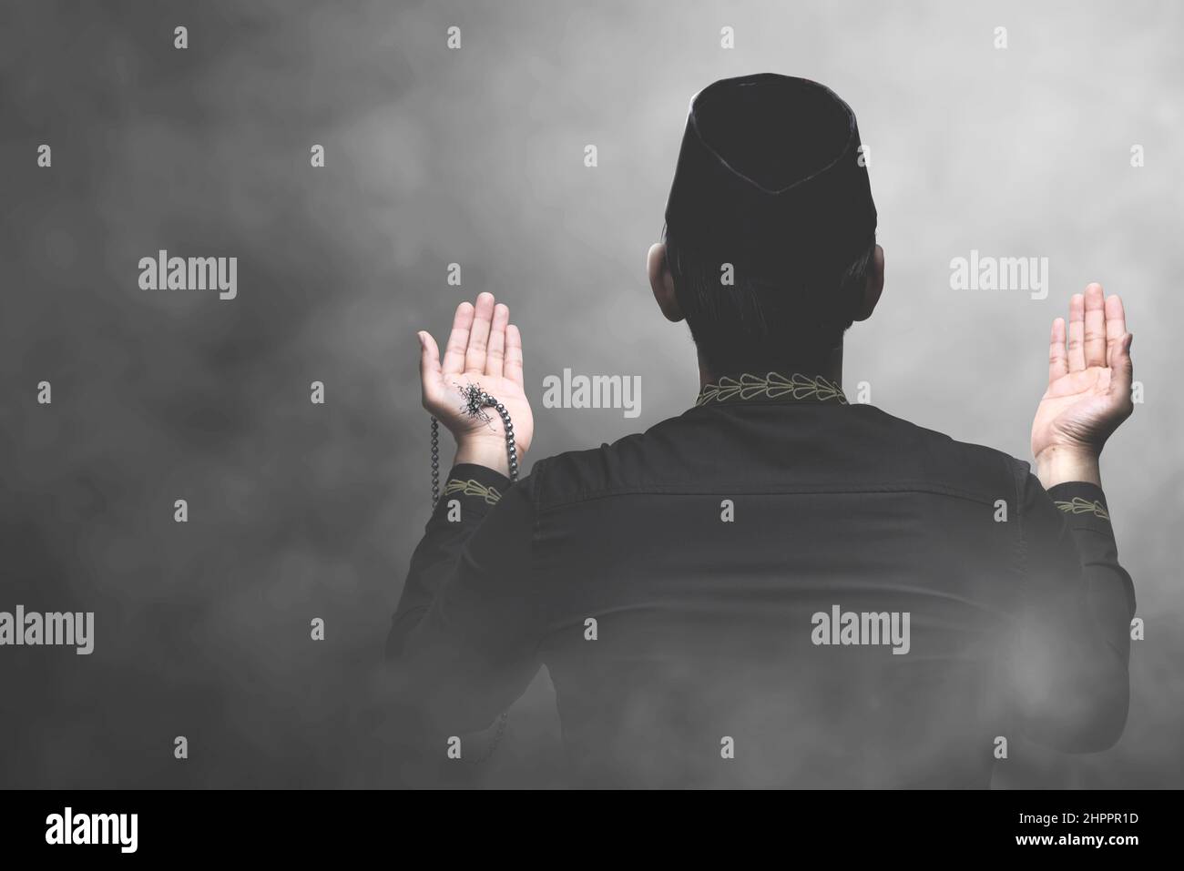 Rear view of Asian Muslim man praying with prayer beads on his hands ...