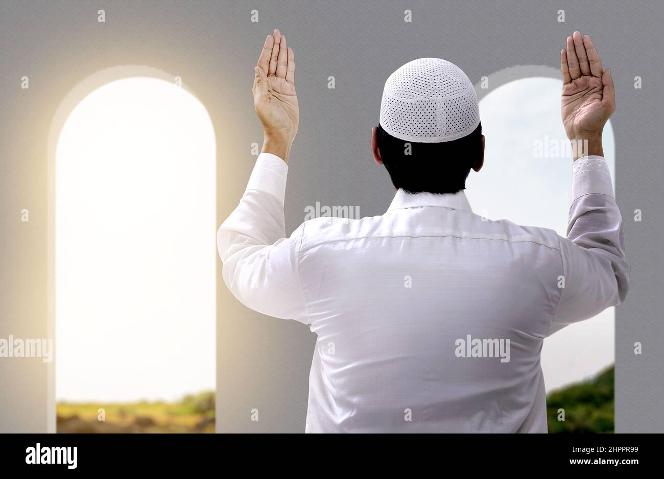 Rear view of Asian Muslim man standing while raised hands and praying ...