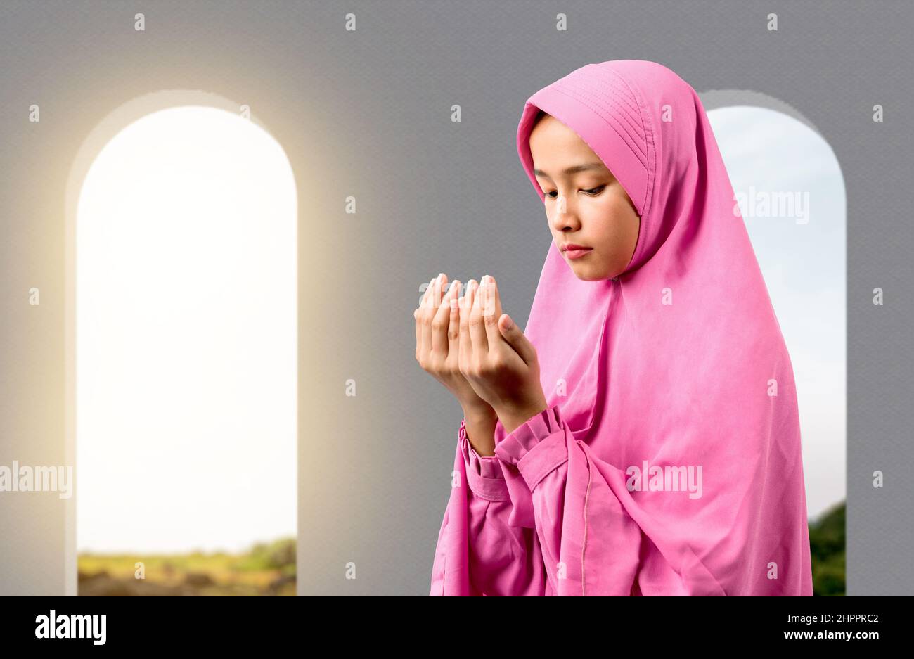 Asian Muslim woman in a veil standing while raised hands and praying on ...