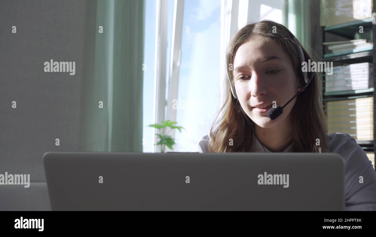 Young woman wearing headphones, communicating online via laptop ...