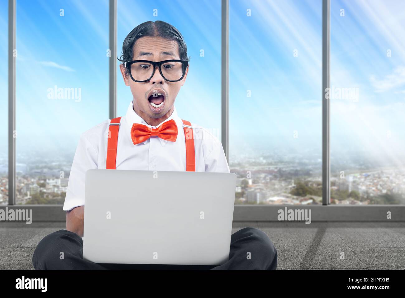 Asian nerd with ugly face sitting while using laptop inside the room ...