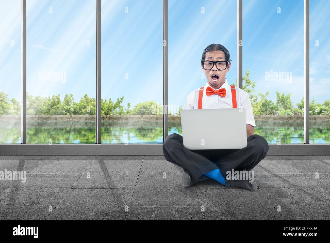 Asian nerd with ugly face sitting while using laptop inside the room ...