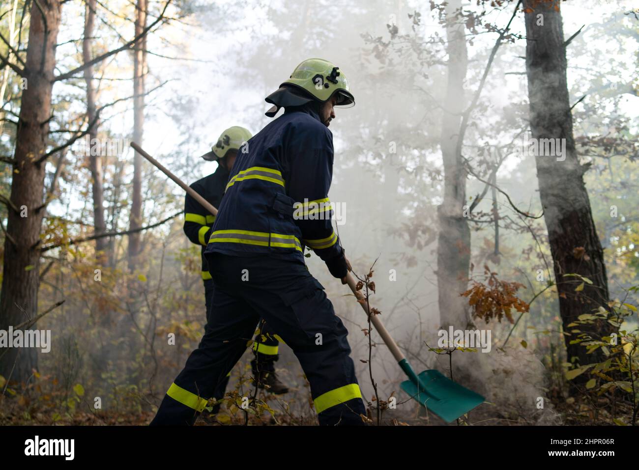 Firefighters men at action, running through smoke with shovels to stop ...