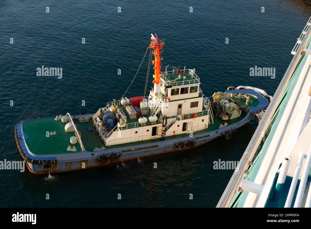 A tugboat gently pushing a large cruise ship and maneuvering it into ...