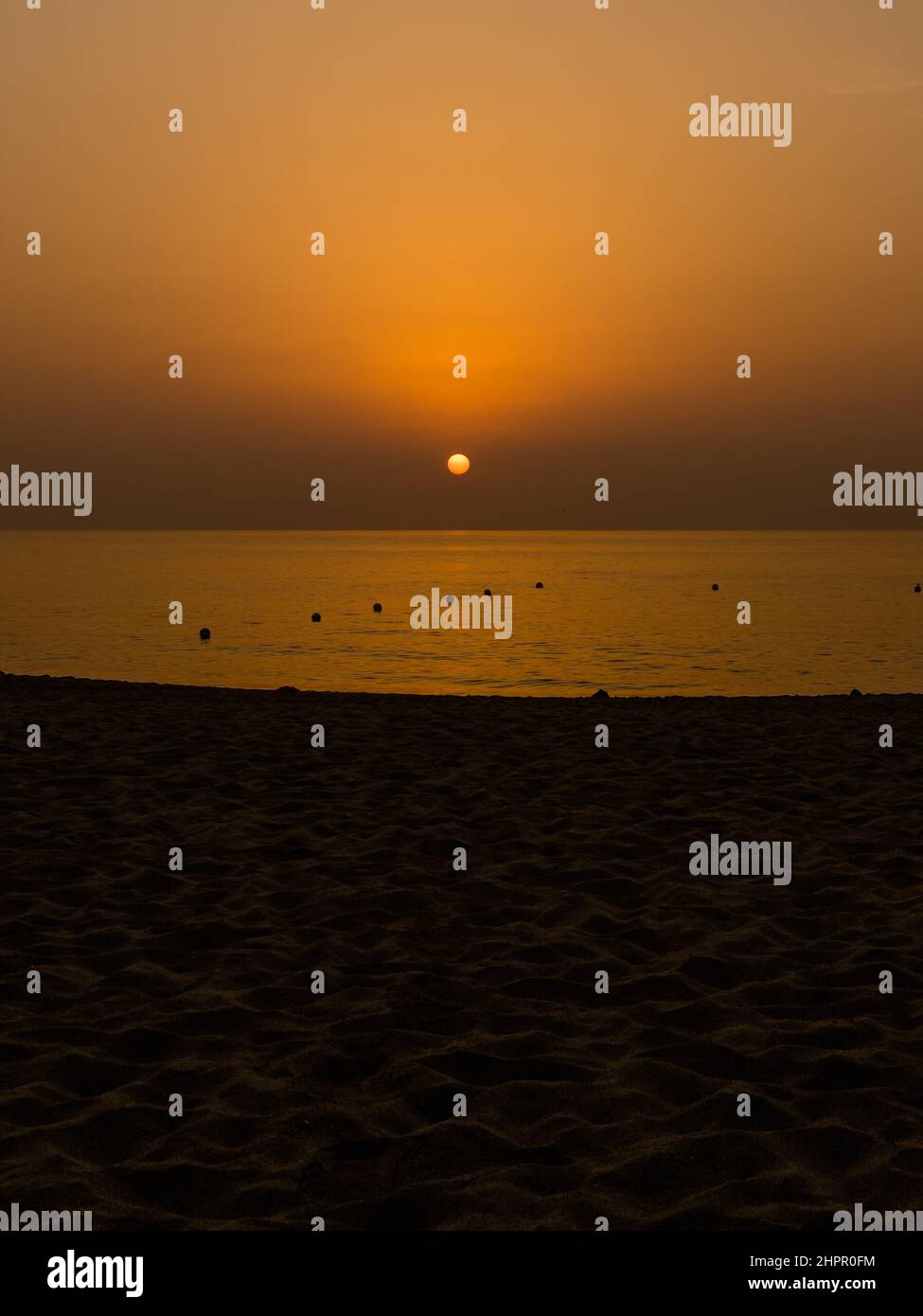 Orange sun slowly rising on the horizon during sunrise with the sand on ...