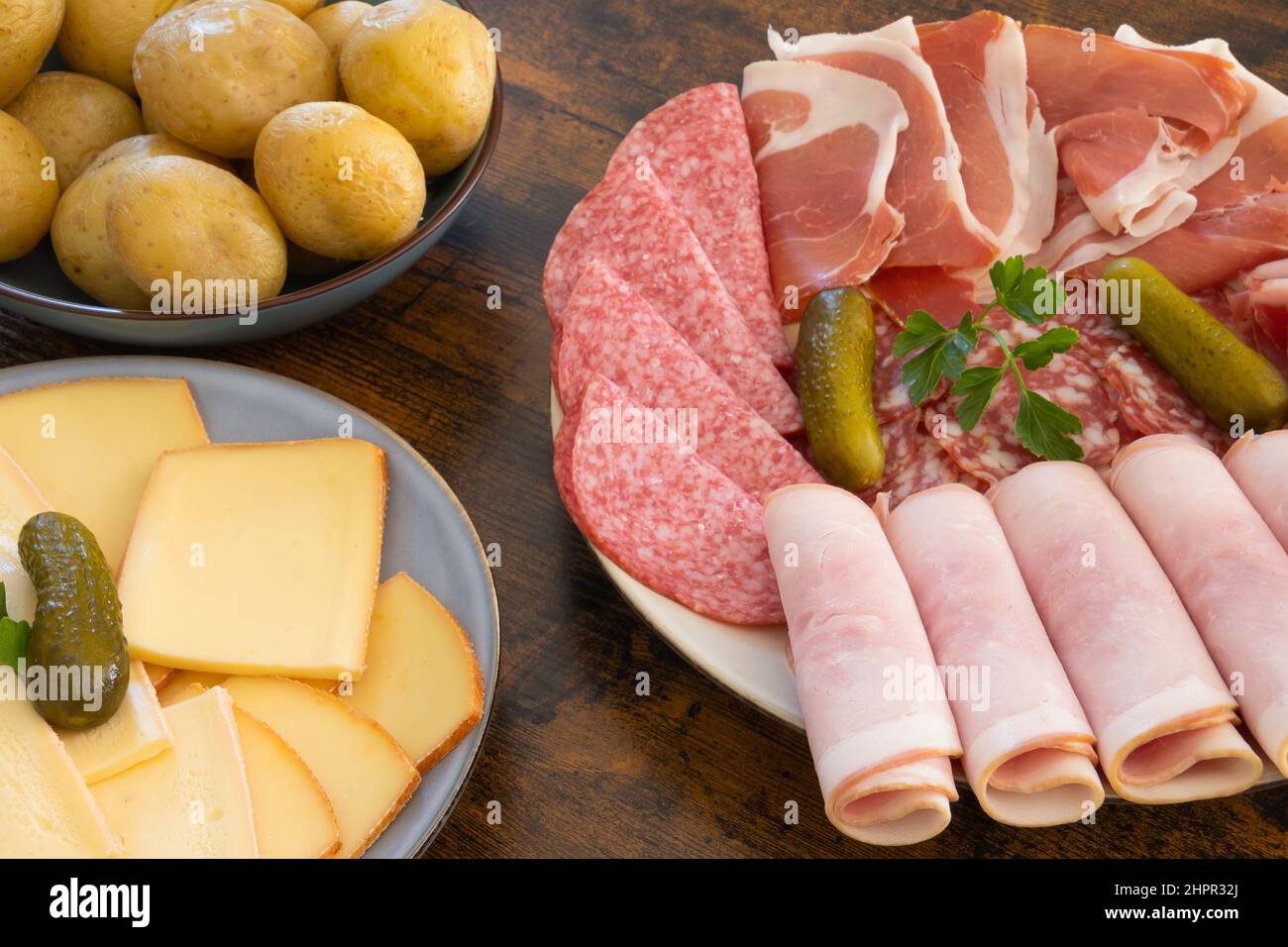 plate of charcuterie with raclette cheese and potato on a wooden table ...