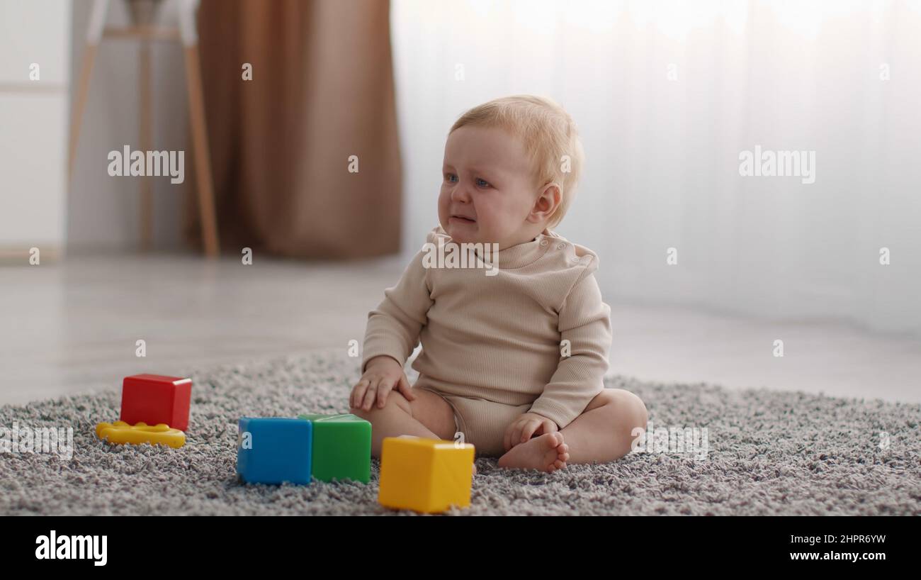 Portrait of cute little baby crying, sitting on floor with colorful ...
