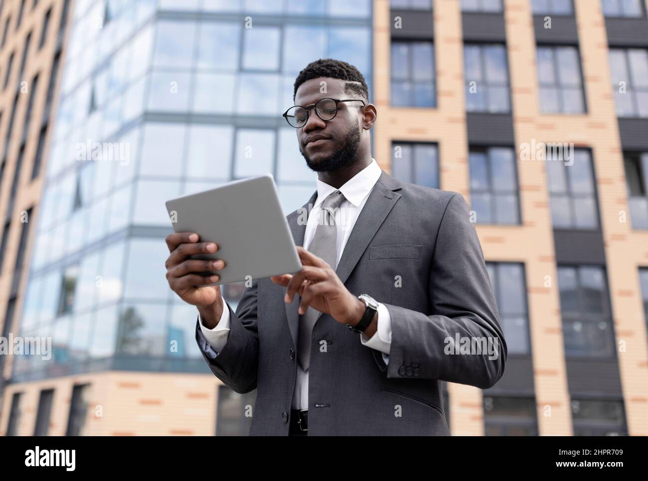 Focused black man in formal wear standing by office building, holding ...