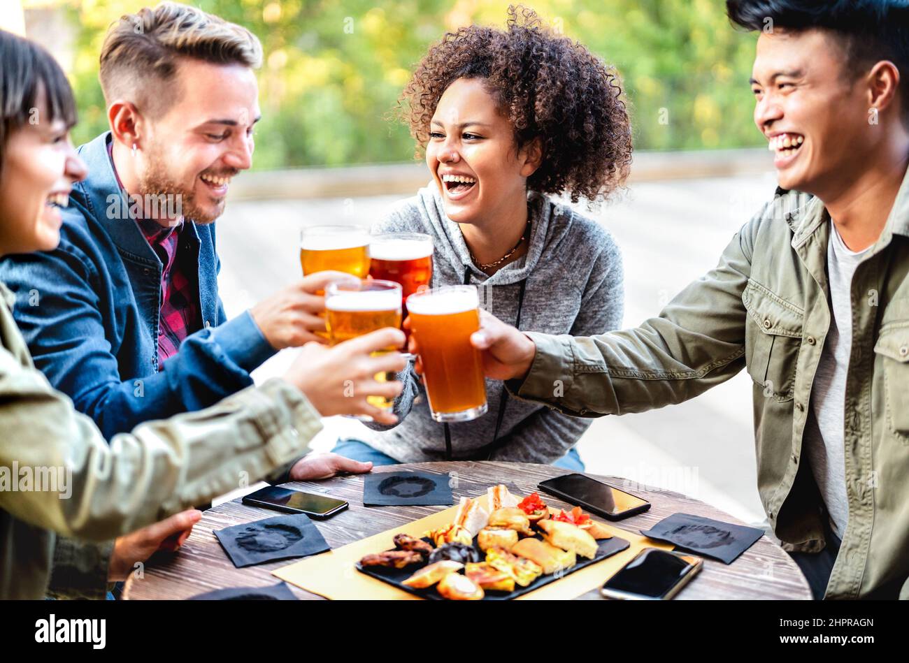 Young multicultural friends drinking and toasting beer at brewery bar ...