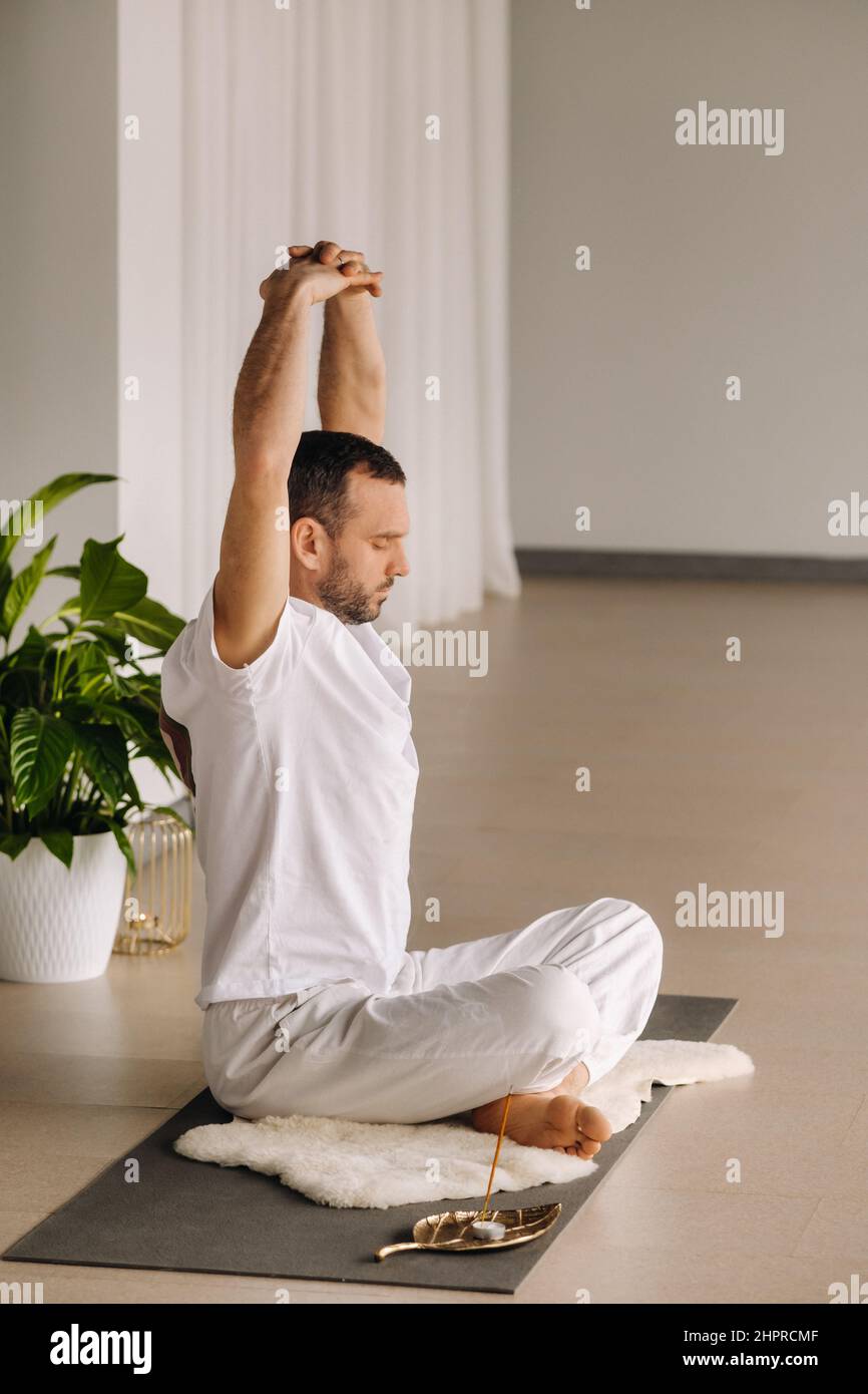 a man in white sportswear is doing yoga with a fitness room. the ...