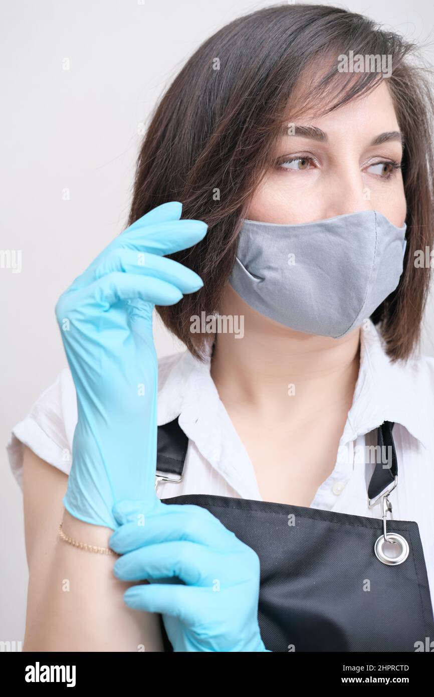 woman wearing apron putting on blue protective gloves. brunette woman ...