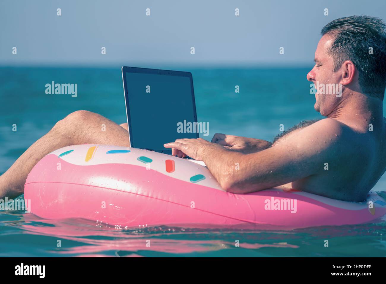 Young man working, using laptop computer on inflatable ring in the ...