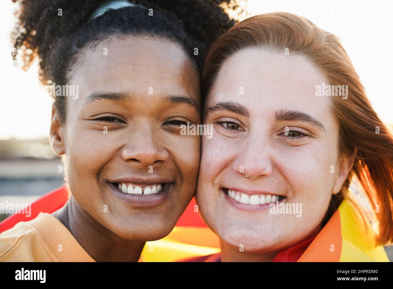Multiracial Women Gay Couple Smiling On Camera Wearing Rainbow Flag